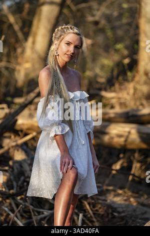 A stunning young woman walks by a creek, her white spring dress swaying ...