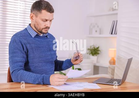 Man paying bills with laptop at wooden table indoors Stock Photo - Alamy