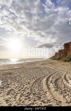 Rocky coastline with red earth, sandy beach and vibrant sky with clouds ...