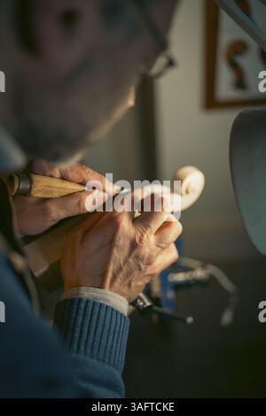 Skilled luthier carefully carving violin scroll with specialized gouge ...