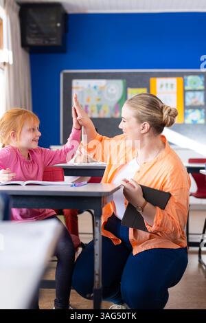 Female teacher and girl high-fiving in classroom, celebrating success ...