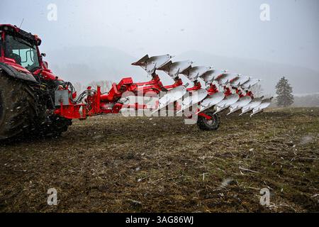 Red tractor pulling plow in field during snowfall, preparing soil for ...
