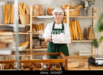 Saleswoman giving cake in white box to male buyer in bakery Stock Photo ...