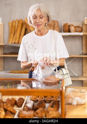 Female shopper selects and places fresh croissants in plastic bag at ...