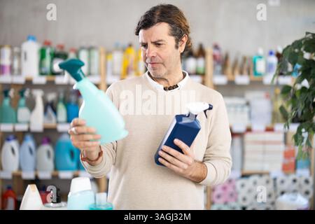 Positive male shopper carefully selects spray glass cleaner for windows ...