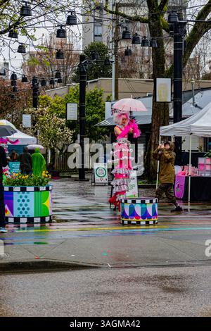 A stilt walker in a pink floral costume with an umbrella, festival ...