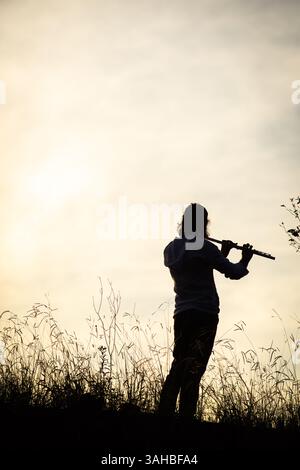 a piper playing a c flute against a hard sun in the background amidst a ...