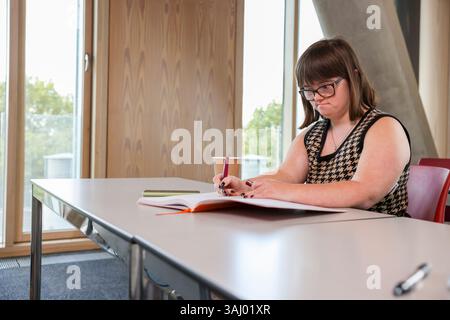 Young woman with down syndrome writing in book on table at home Stock ...