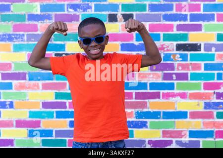 Smiling boy in sunglasses flexing arm muscles in front of colorful ...
