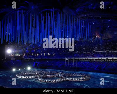 Performers dressed in mirrored costumes form the Olympic Rings, during ...
