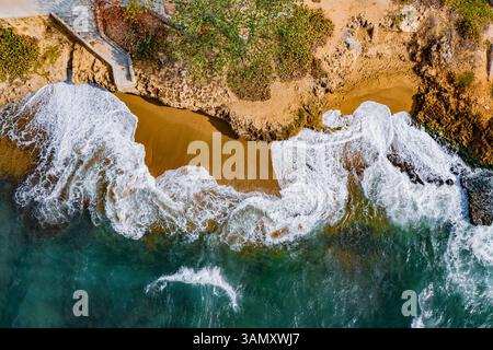 The aerial view of ocean waves touching the dandy shore on a sunny day ...