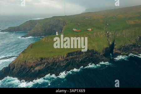 Aerial view of Akraberg Lighthouse on a rugged cliff by the serene ...