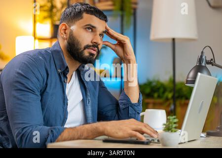side view of tired hispanic freelancer sitting at work desk near laptop ...