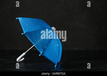 Mini blue umbrella with water drops on black background Stock Photo - Alamy