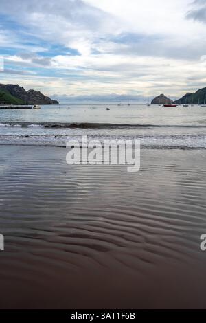 The black sand beach of Taiohae Bay in Nuku Hiva, Marquesas Islands, is ...