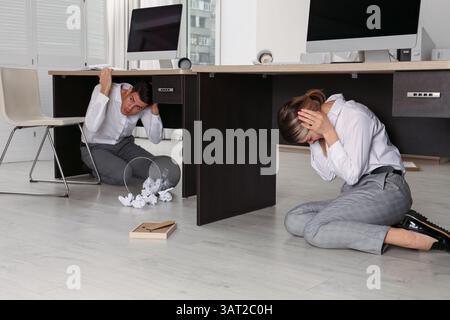 Scared employees hiding under office desks during earthquake Stock ...