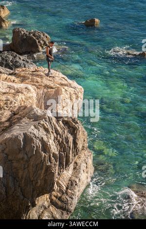 Italian man with a fishing rod, standingon a rock and fishing in the ...