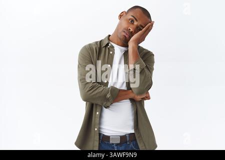 Sad and bored man lean face on hand, looking at camera empty-headed ...