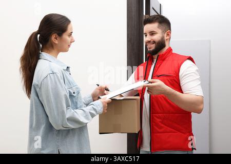 Smiling courier with box and receiver signing for delivered parcel ...