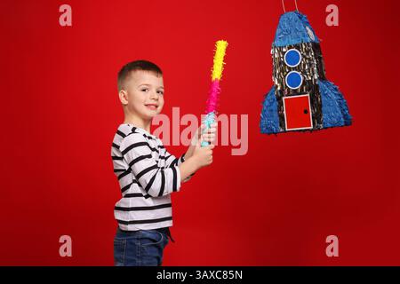 Happy boy breaking rocket shaped pinata with stick on light blue ...