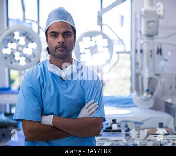 Standing male surgeon crossing arms in operating room, with surgical ...