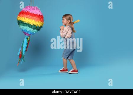 Happy girl breaking bright pinata with stick on light blue background ...