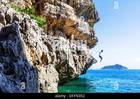 A local Filipino leaps from a rocky cliff into the vibrant blue sea at ...