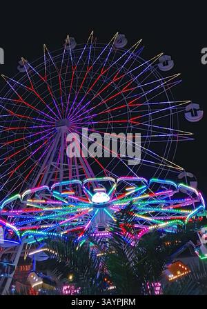 A vibrant Ferris wheel illuminated with dazzling neon lights spins ...