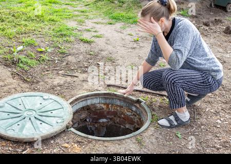 A woman looks into an open septic tank to check the level of sewer ...