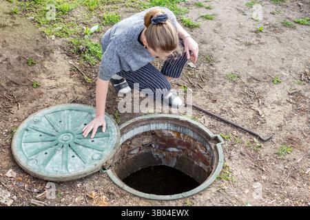 A woman looks into an open septic tank to check the level of sewer ...