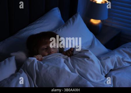 Scared boy hiding under duvet in bed at night Stock Photo - Alamy