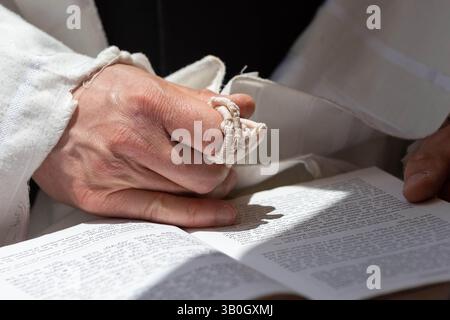 An Orthodox, Jewish man holds tzitzit strings while reciting the Shema ...