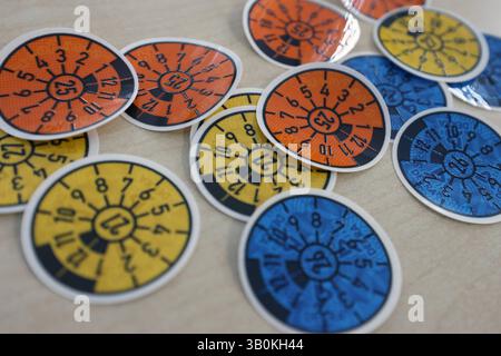 Tuev Tüv Plaketten in den Farben gelb, blau und orange liegen auf einem ...