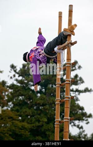 Traditional Japanese fireman performing stunts atop a bamboo ladder ...