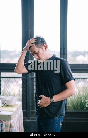 Asian man holding stomach in pain at home for abdominal discomfort ...