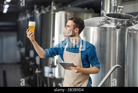 Beer quality control. Man with digital tablet looking at glass of beer ...