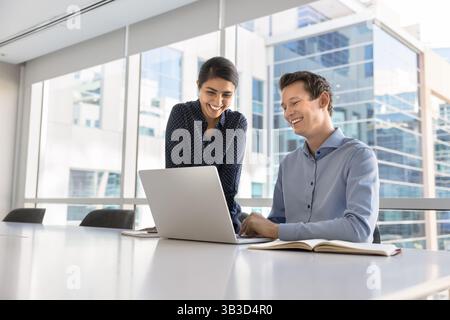 Caucasian man looking at laptop with Indian man and smiling Stock Photo ...