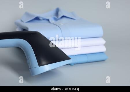 Upright steamer and stack of folded clothes on white table against ...