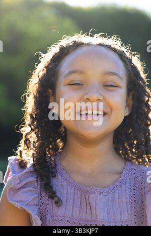 smiling girl in bright dress and sun hat drinking water on warm summer ...