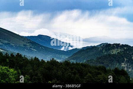 Misty mountain landscape with clouds hovering over rocky peaks and a ...