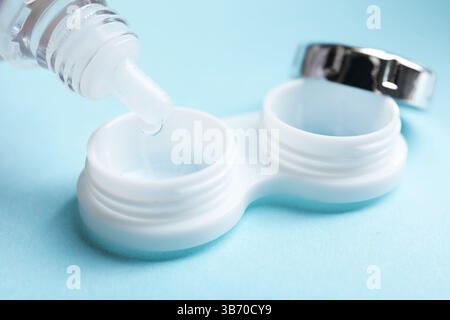 Dripping contact lens solution from bottle into case on light blue ...