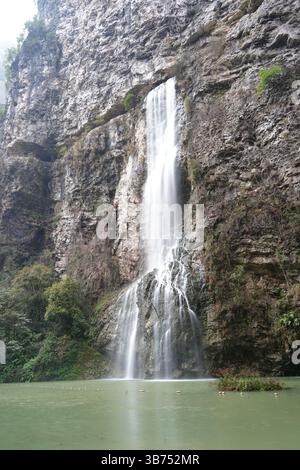 Waterfall cascading down a rugged mountain cliff amidst lush greenery ...