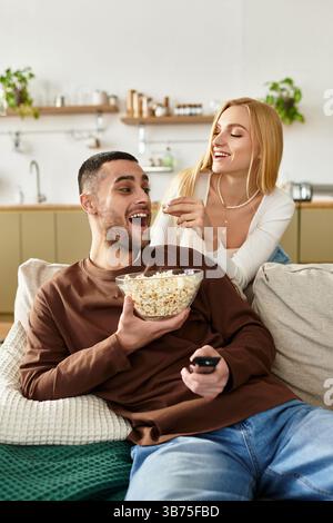 Joyful couple shares popcorn while watching a show in their warm and ...