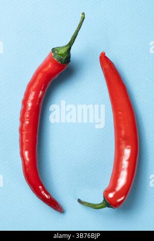 Two fresh red chili peppers arranged diagonally on light grey and beige ...