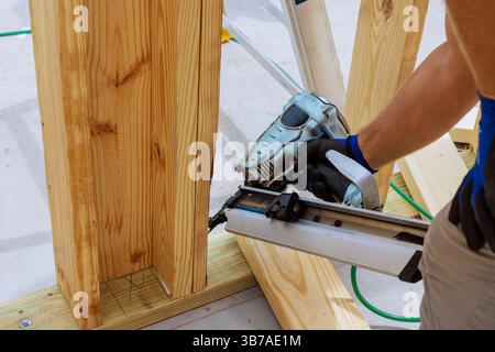 Frame worker operates power hand saw on wooden beam in wooded area ...