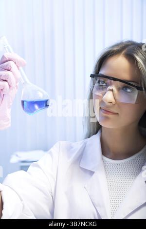 Female researcher look at retort with blue liquid Stock Photo - Alamy