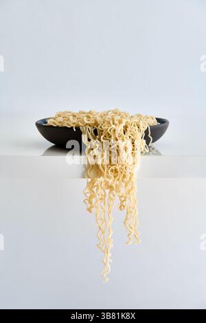 Cooked instant noodles overflow and spill from full bowl into table ...