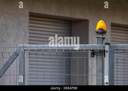 Orange warning lamp hanging on a metal electric sliding gate, warning ...
