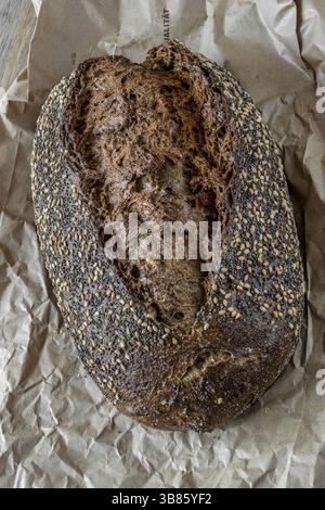 A loaf of brown bread with grains of cereals on a wooden cutting board ...