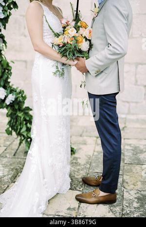 The groom holds the bride's hand, in the background a wedding bouquet ...
